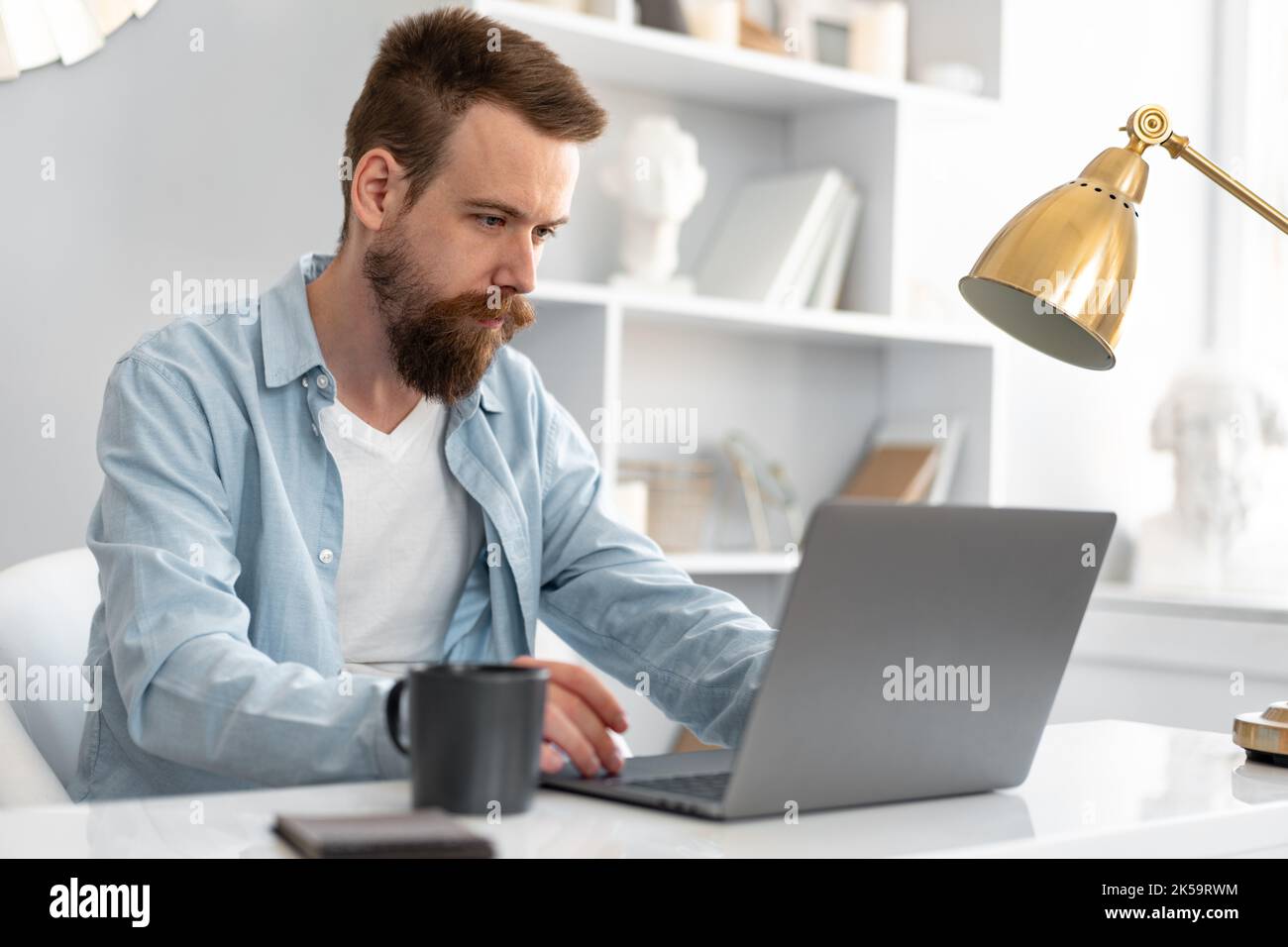 Stylish bearded man working on laptop from home sitting at the table ...