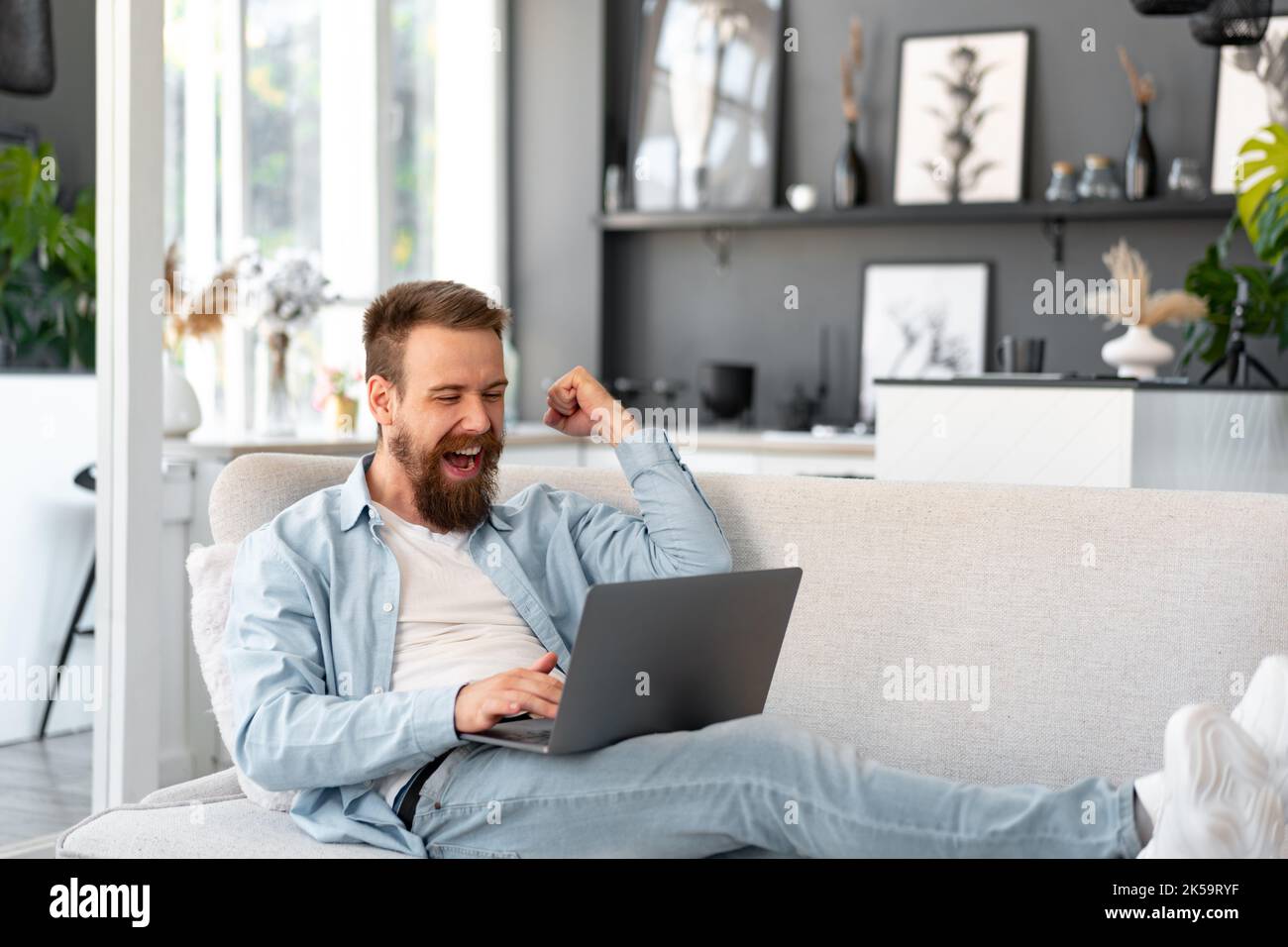 Young bearded man sitting on sofa at home using laptop computer Stock ...