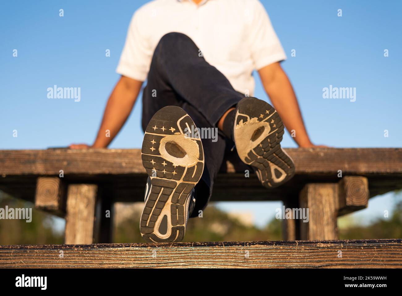 A man wearing running shoes with worn-out outsole is sitting on a bench ...