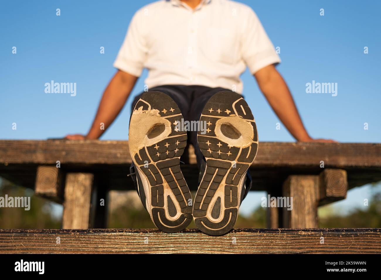 A man wearing running shoes with worn-out outsole is sitting on a bench ...