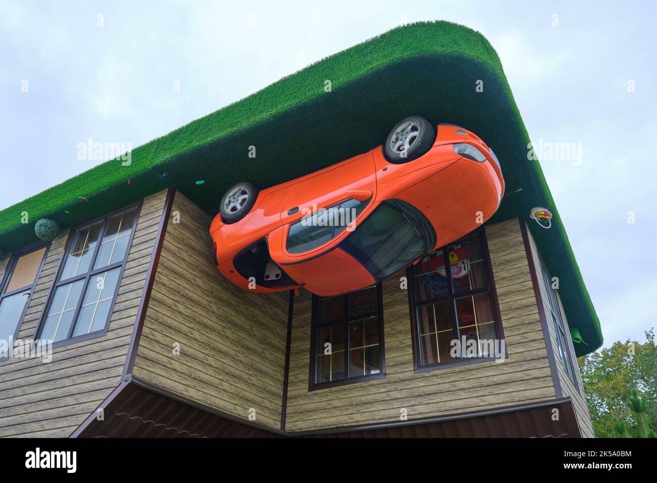 A red coupe car, automobile, mounted, parked at an upside down house ...