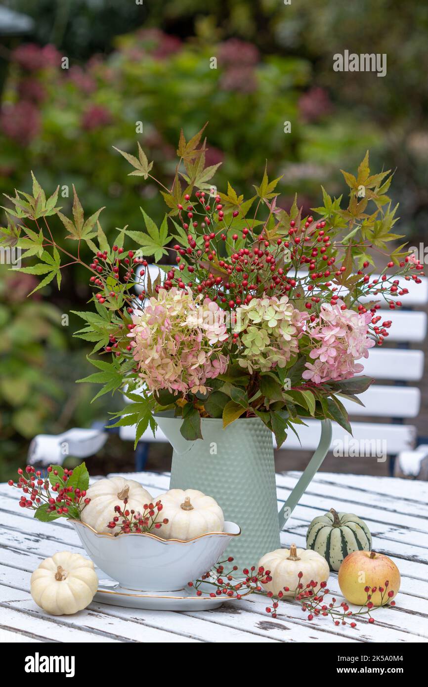autumn bouquet of hydrangea flowers, rose hips and maple leaves in ...