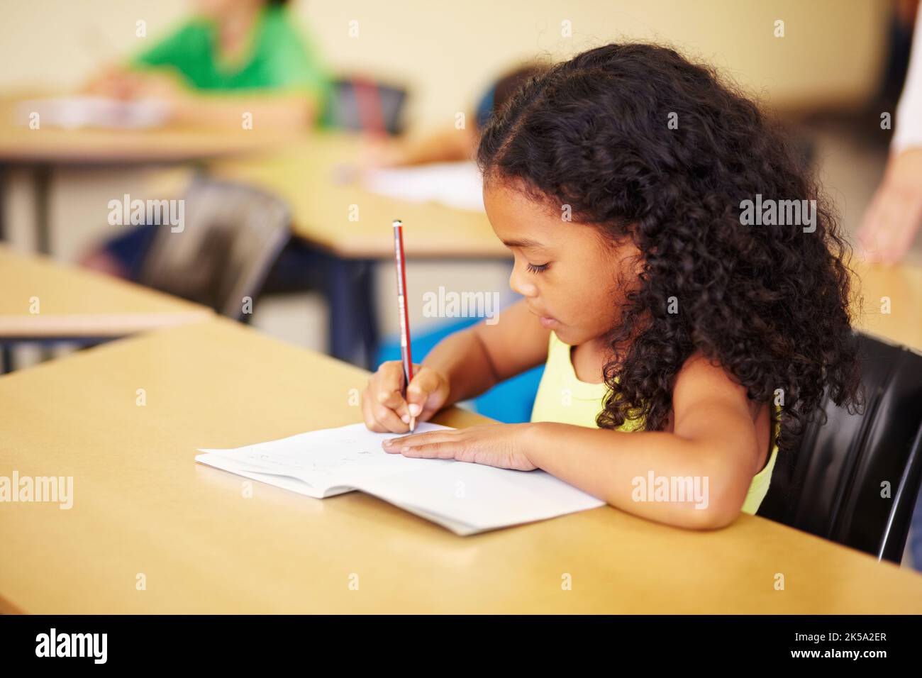 Eager to learn. A cute little girl doing her homework in the classroom ...