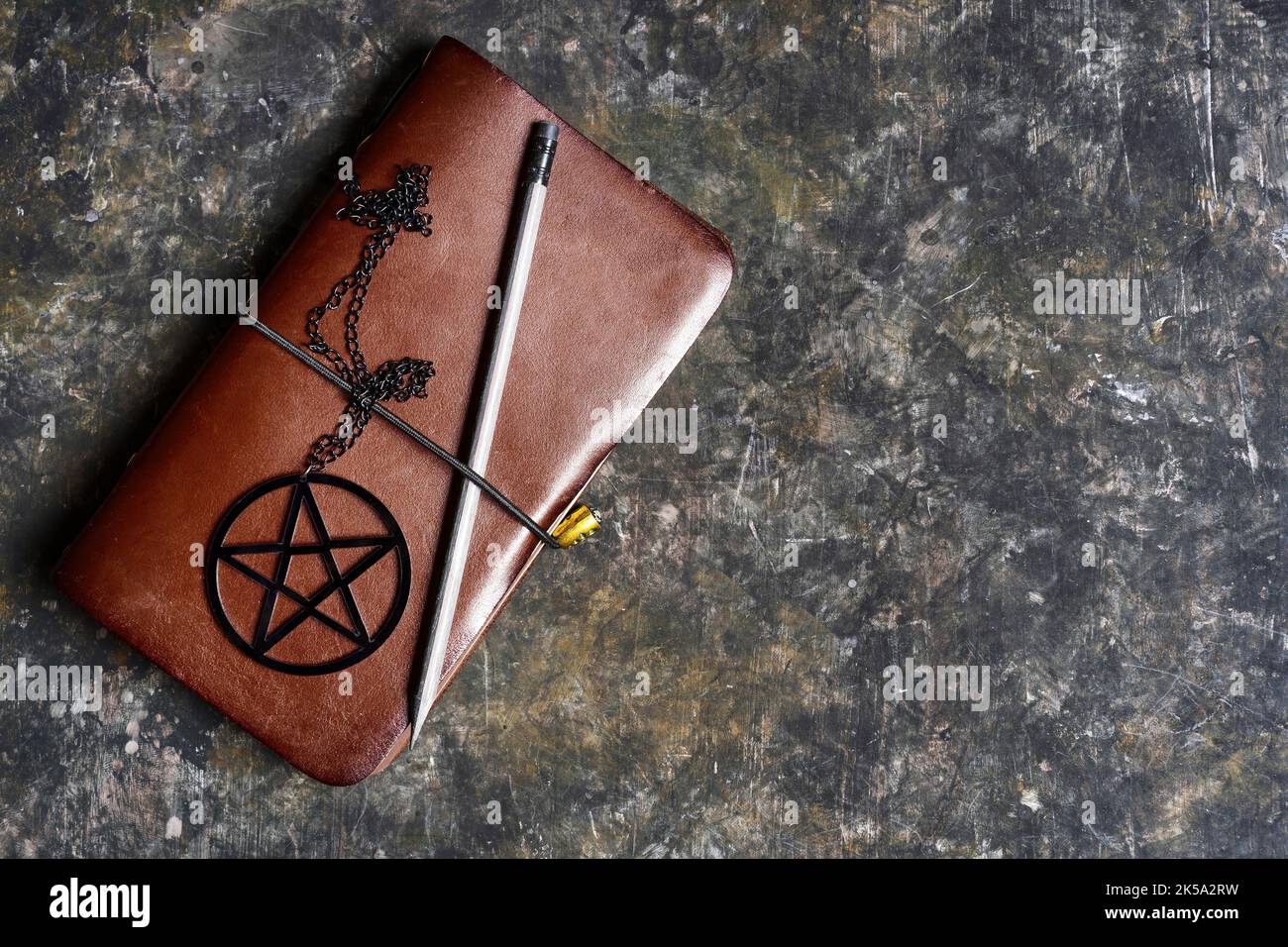 Brown leather pagan notebook with black pentagram and pencil on a dark ...