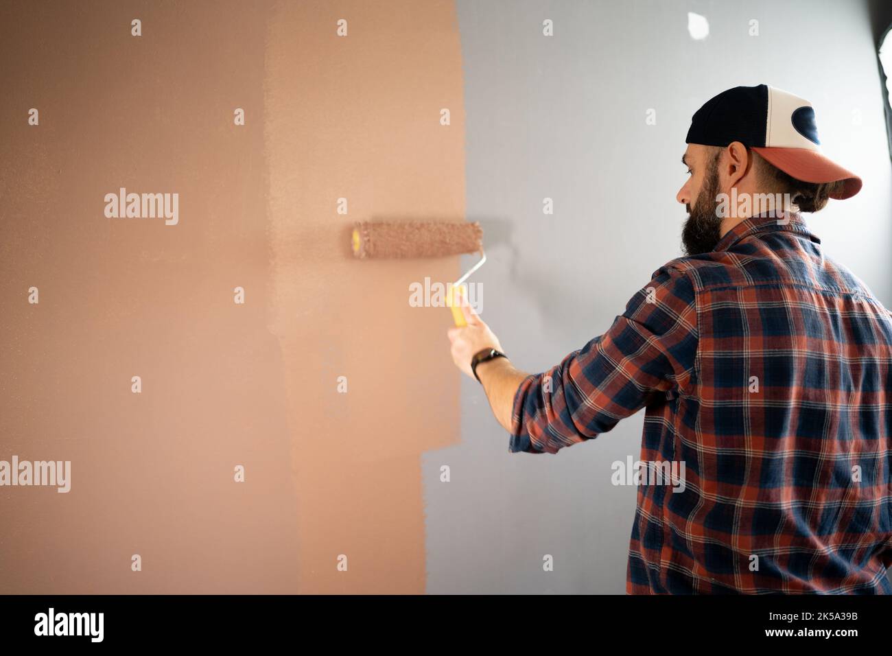 handsome young bearded painter in baseball cap and plaid shirt painting ...