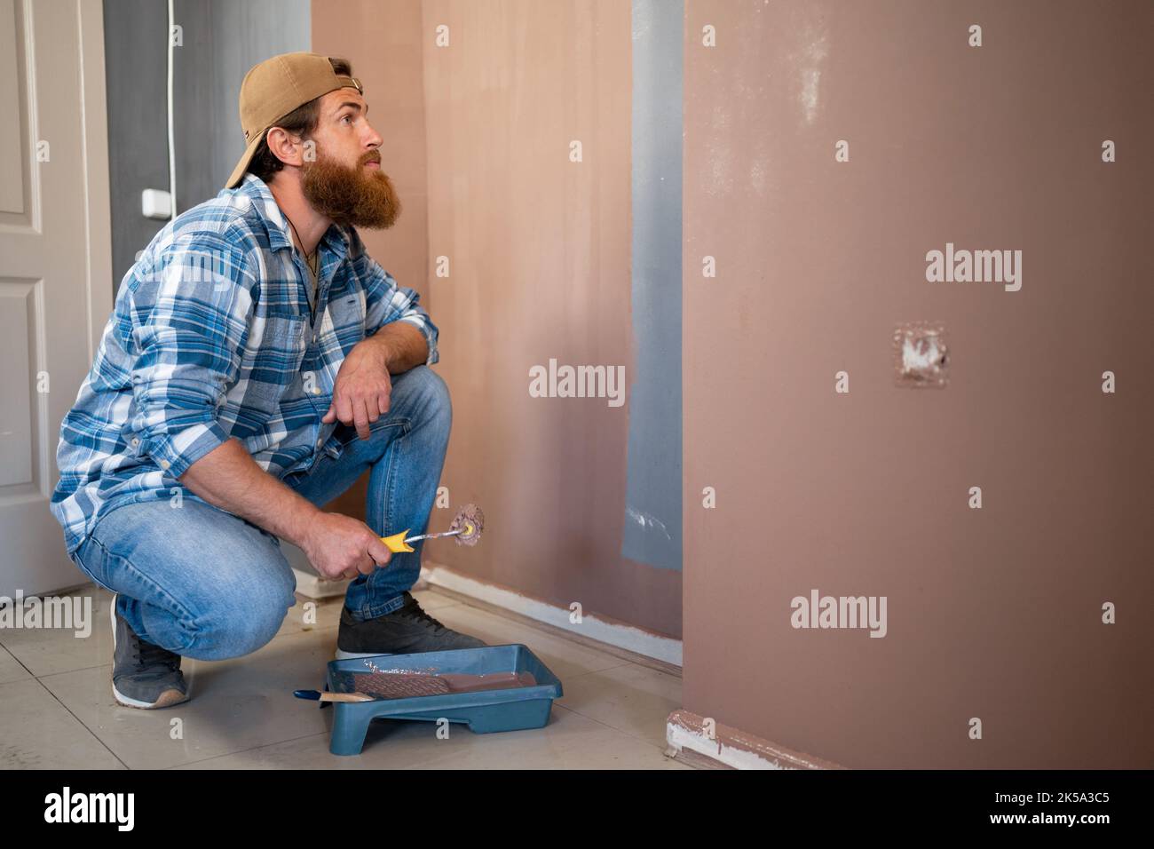 Doubting house painter thinks while sitting with a roller near the wall ...