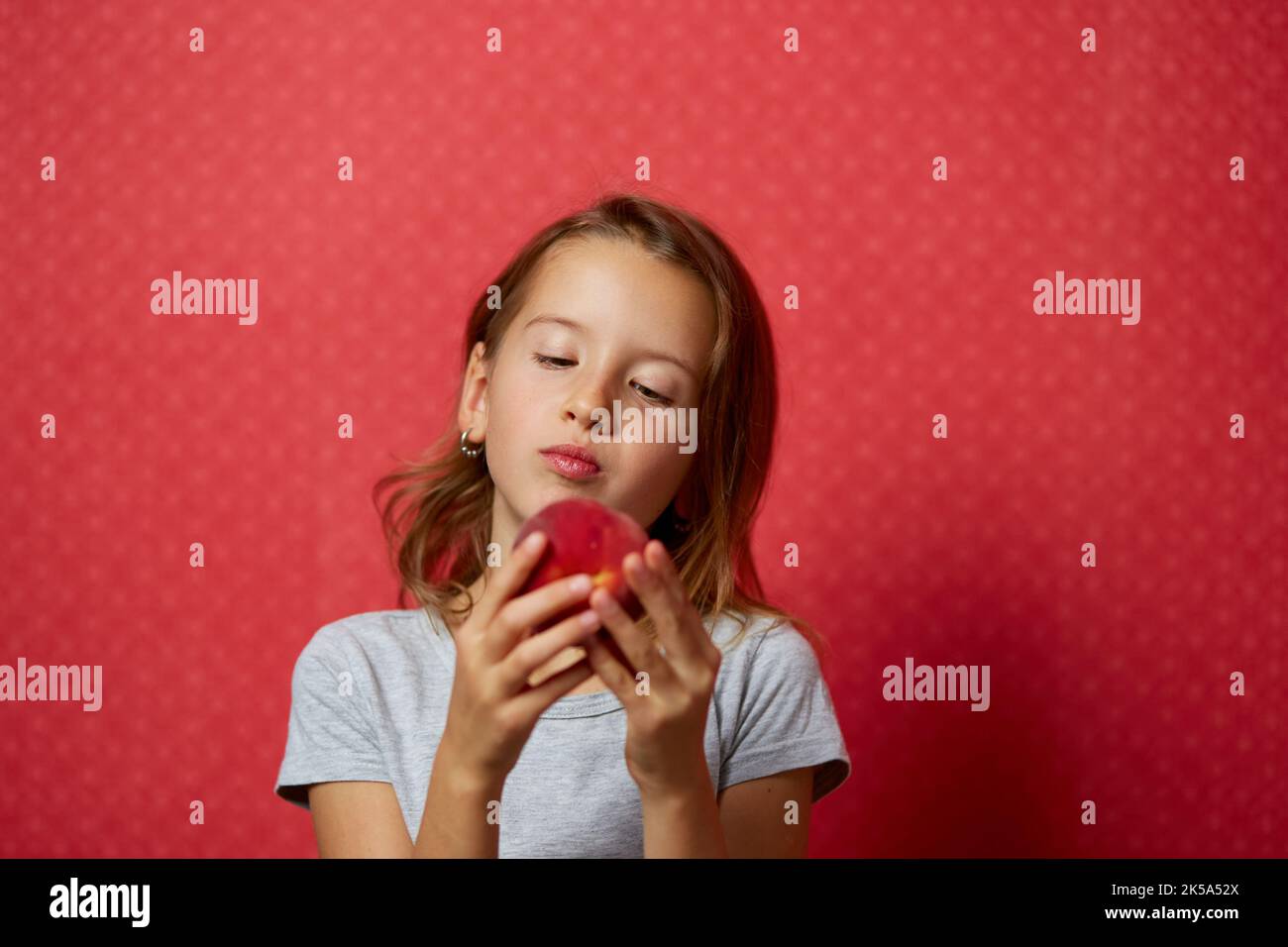 Portrait happy girl eats a peach on a red background, bites a juicy ...