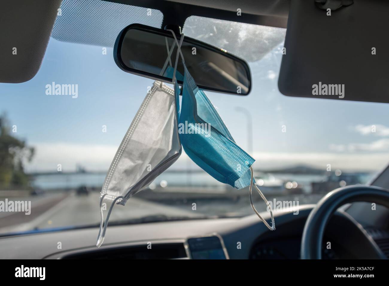 Facemask hanging on the mirror inside a car, driving on the moterway in ...