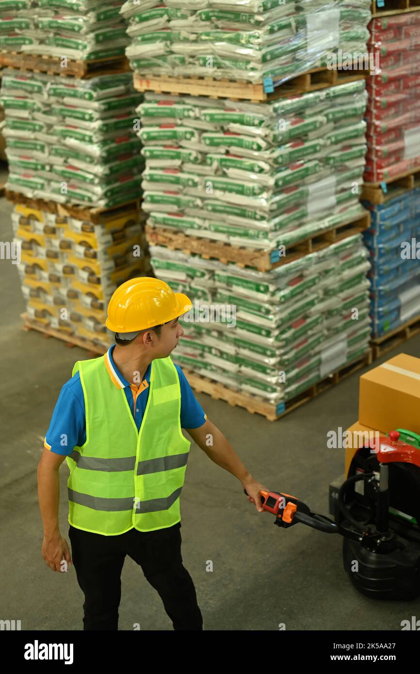 Overhead view of male worker wearing hardhat and vests pulling pallet ...