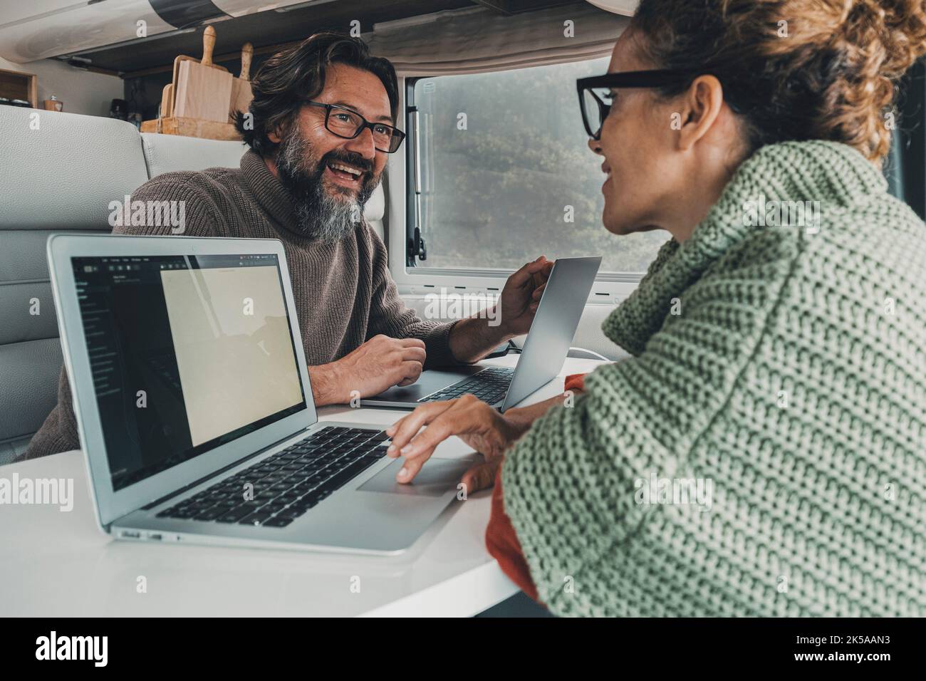 Digital nomad young couple working together inside a camper van using ...