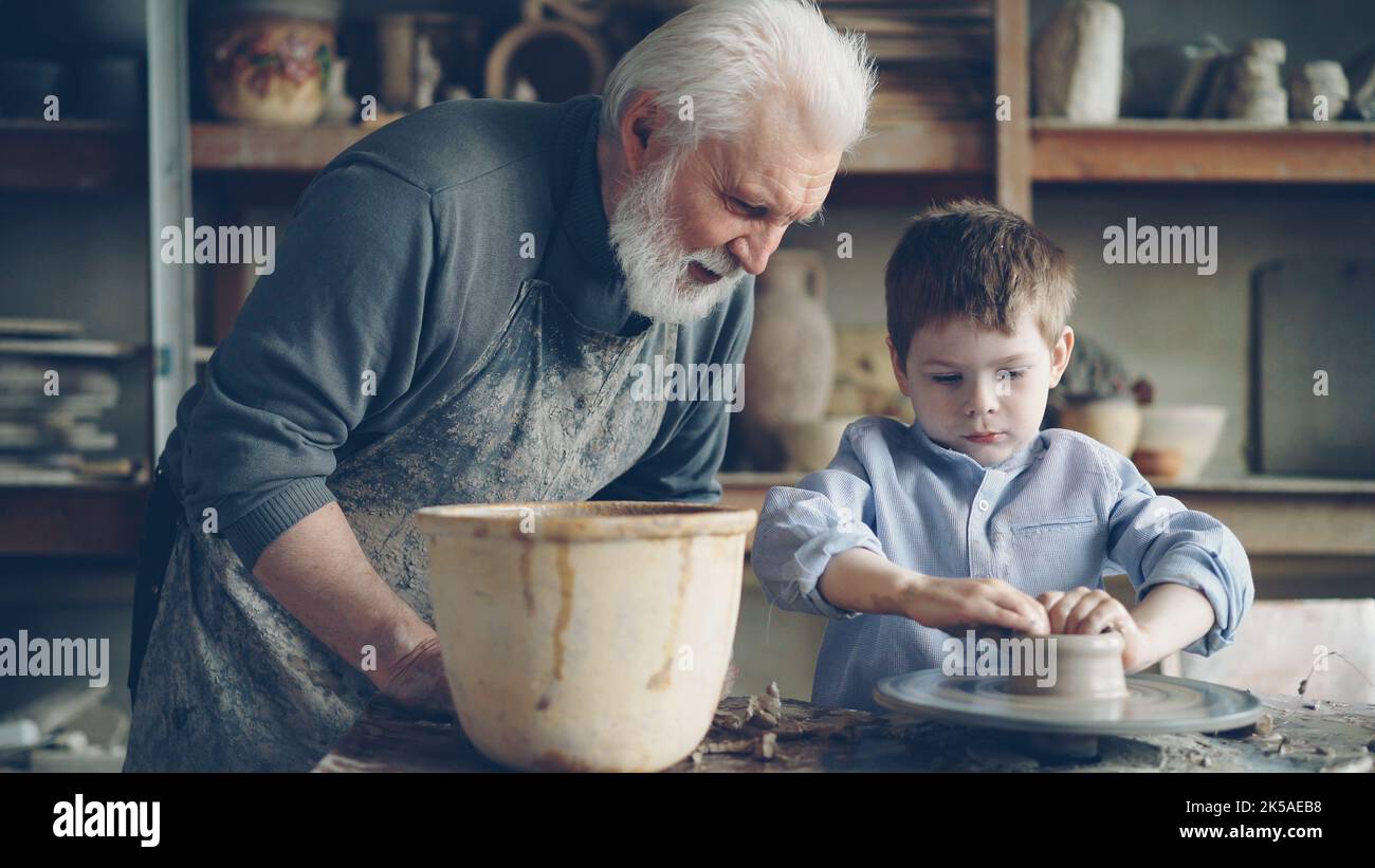 Concentrated young boy is molding clay into ceramic pot on spinning ...