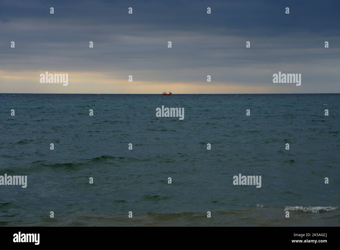 Far out to sea a small trawler is busy fishing under darkening storm ...