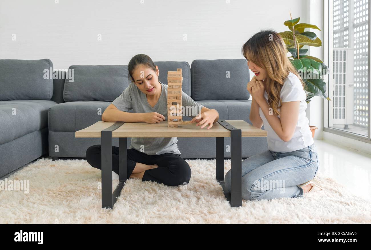 Two asian woman enjoy playing Jenga wooden blocks game in the living ...
