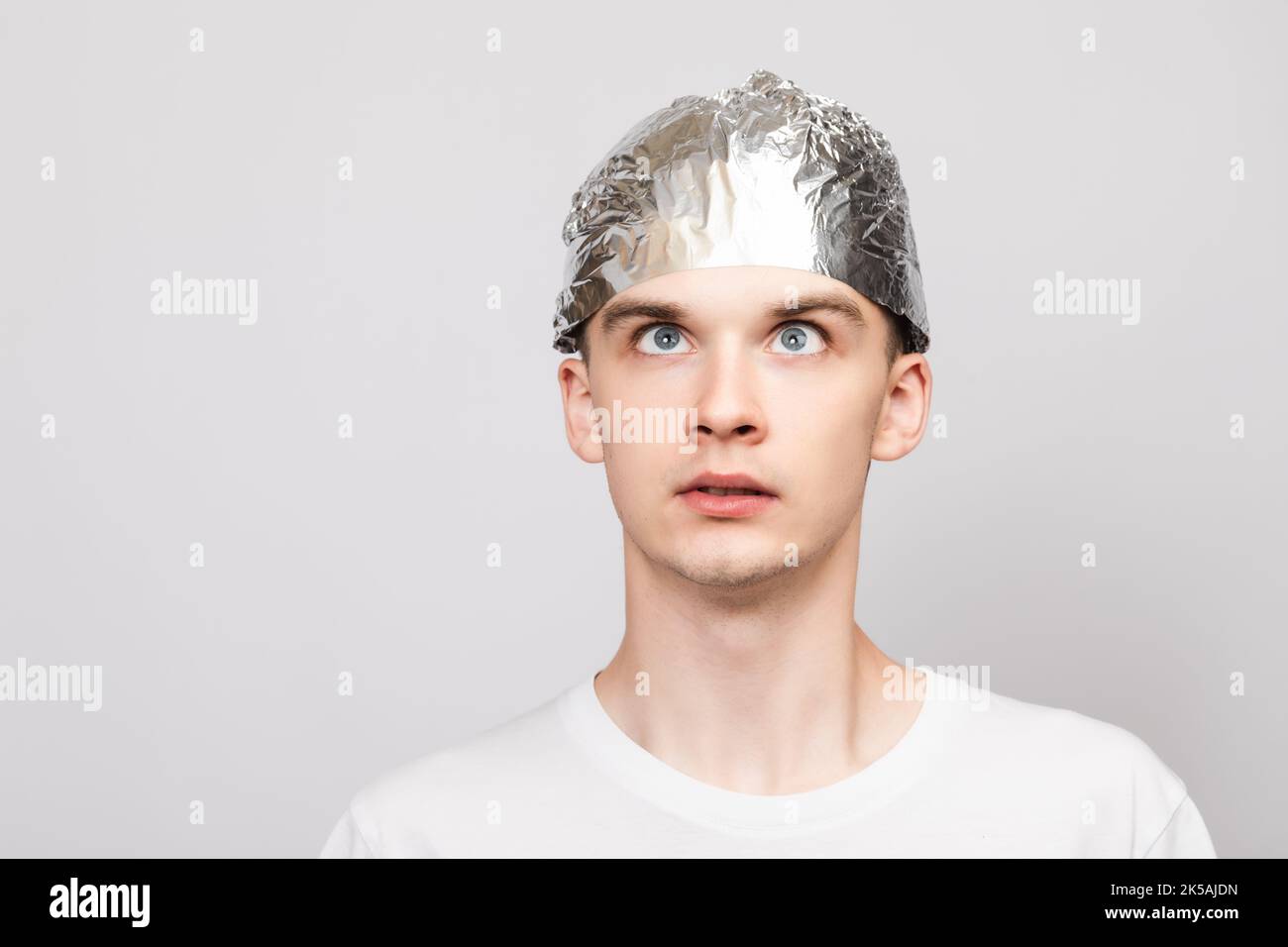Portrait of anxious young man wearing tin foil hat looking up ...