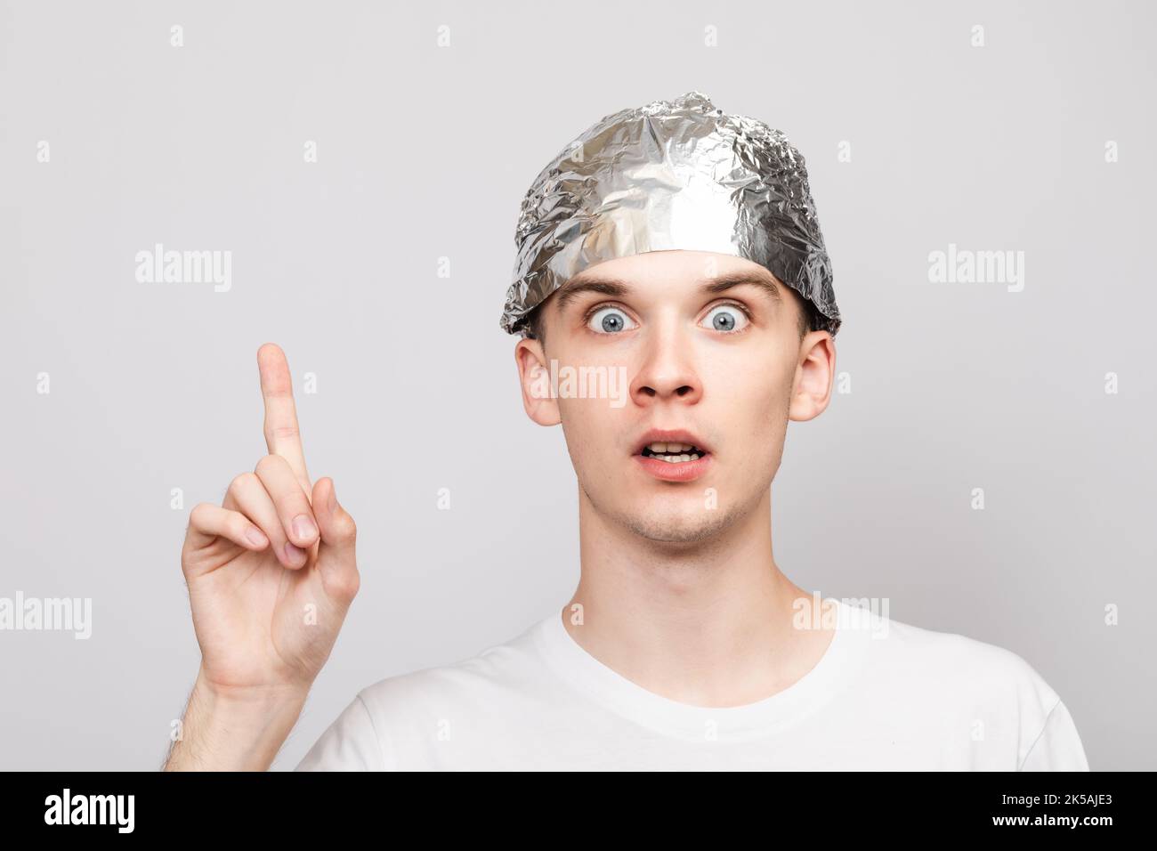 Portrait of anxious young man wearing tin foil hat pointing his finger ...