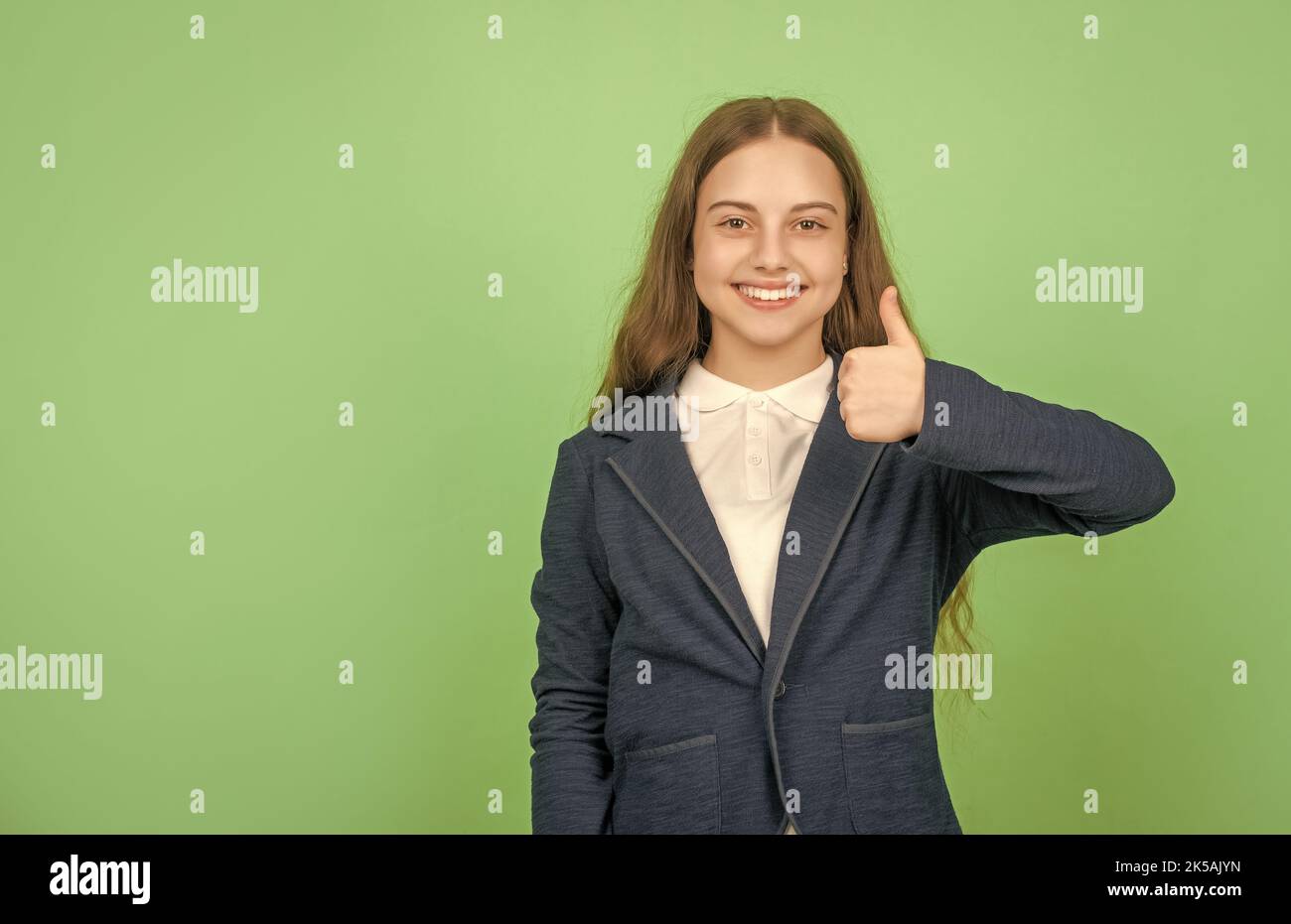 happy kid in school uniform showing thumb up on green background with ...