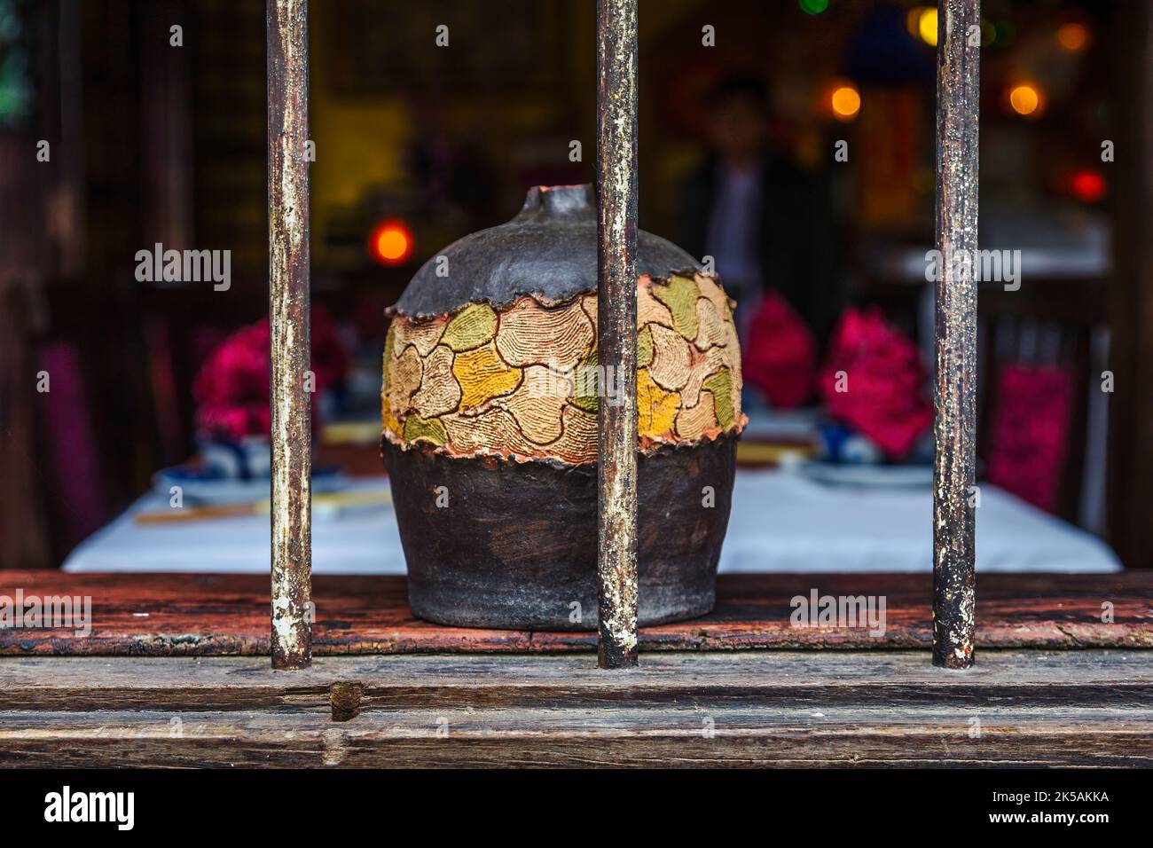 From outside looking in through window bars sits a lone ceramic bottle ...