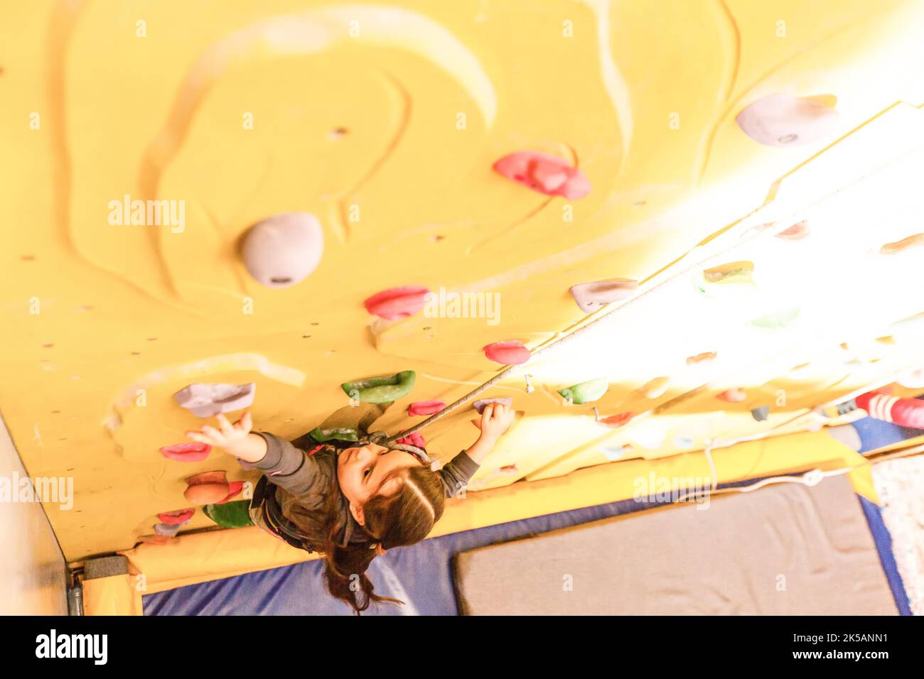 Little baby girl with funny hear style climbing vertical wall and man ...