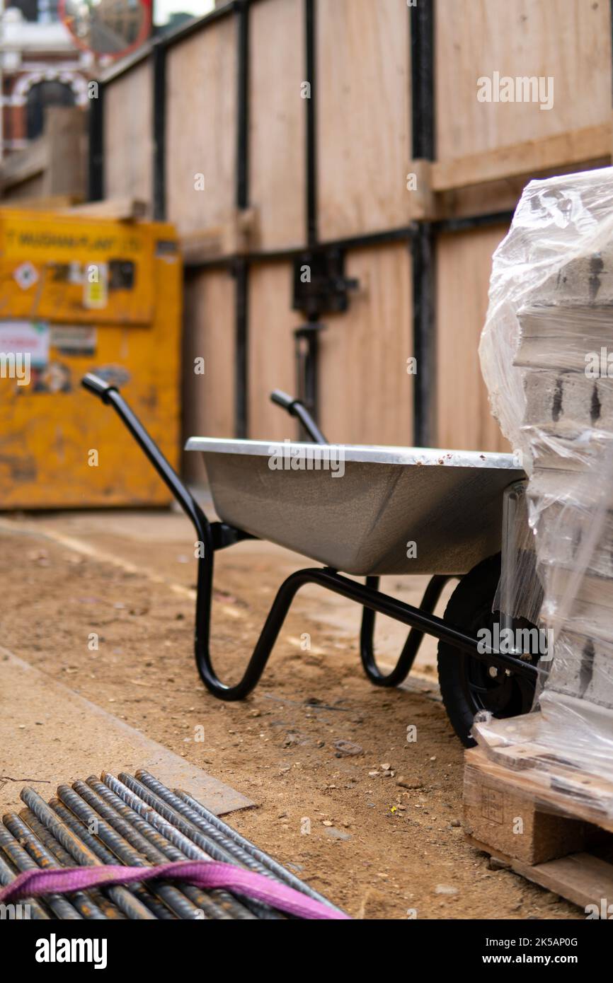 Wheel barrow on construction site with timber hoarding in background ...