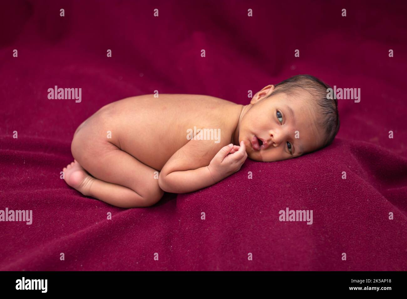 newly born baby laying on red velvet cloth with cute facial expression ...