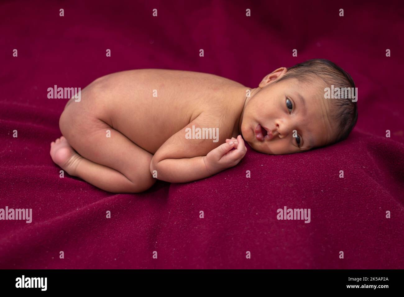 newly born baby laying on red velvet cloth with cute facial expression ...