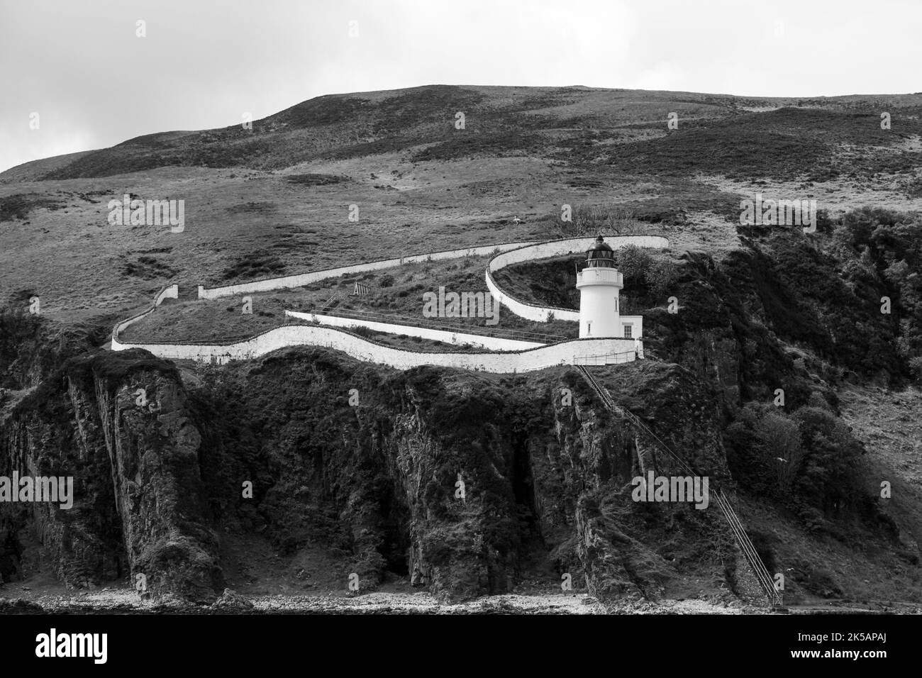 An aerial grayscale shot of a lighthouse on a cliff overlooking an ...
