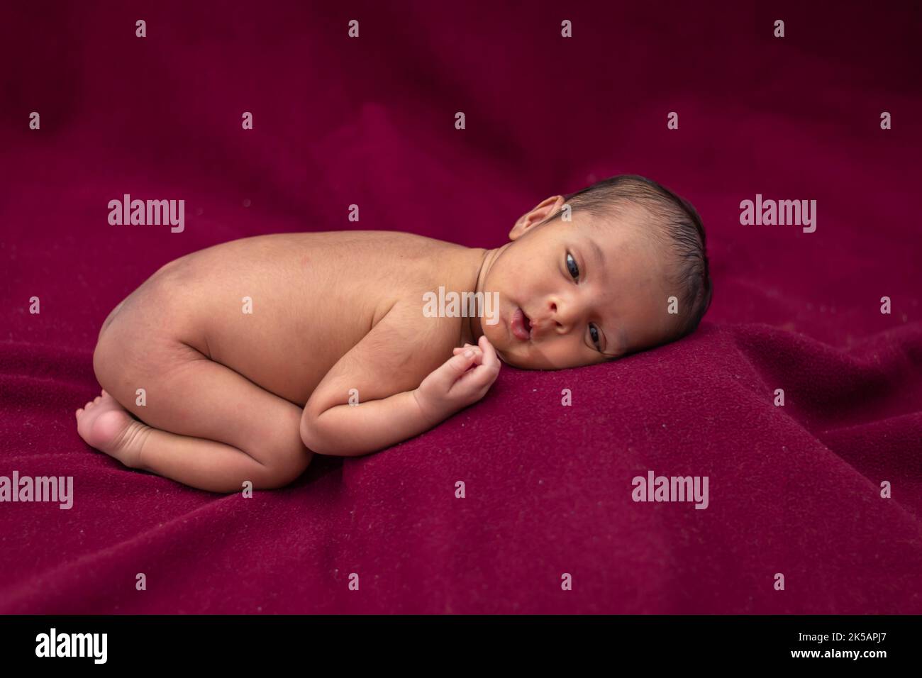 newly born baby laying on red velvet cloth with cute facial expression ...
