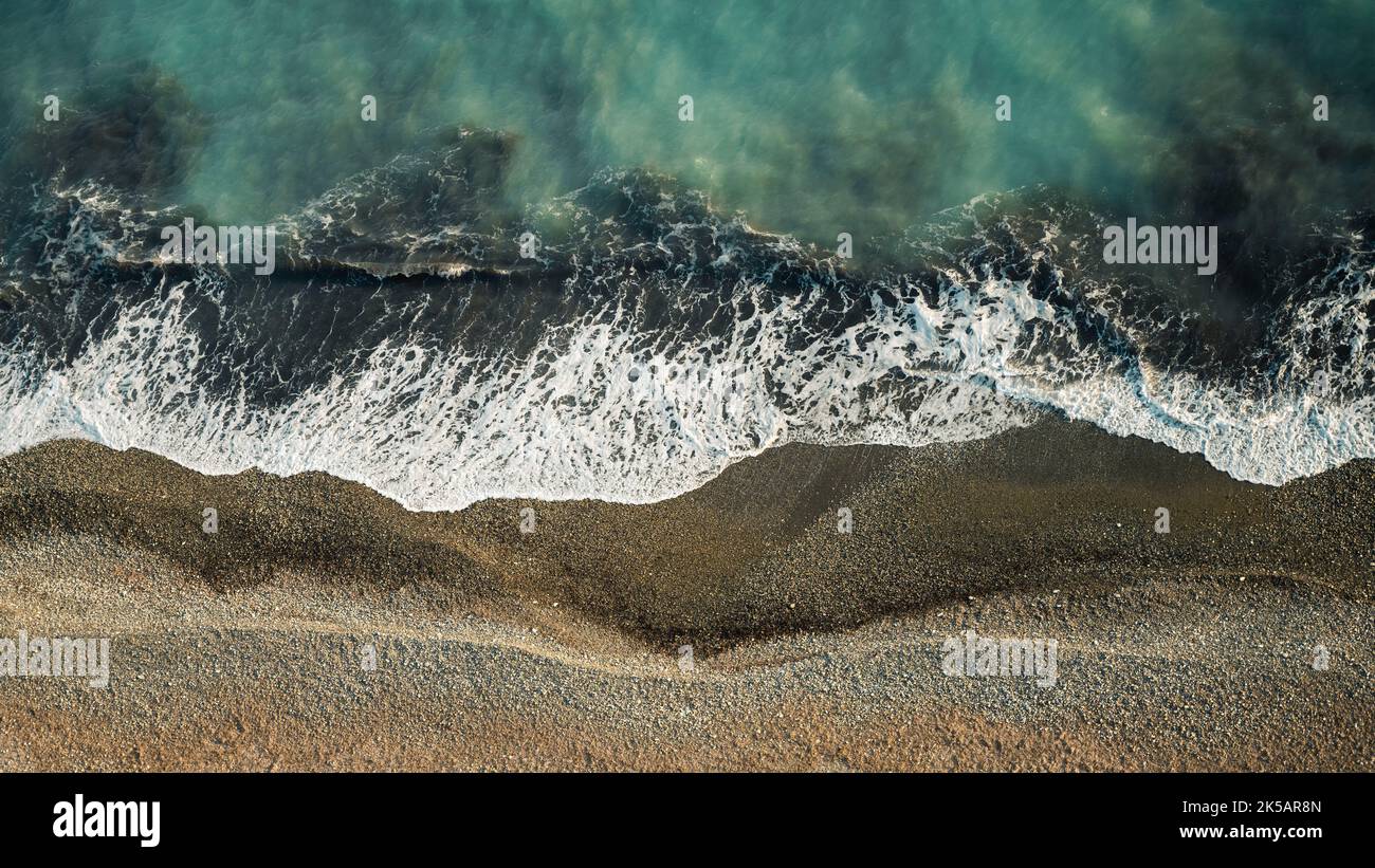 A mesmerizing aerial top-view of the foamy sea waves washing the shore ...