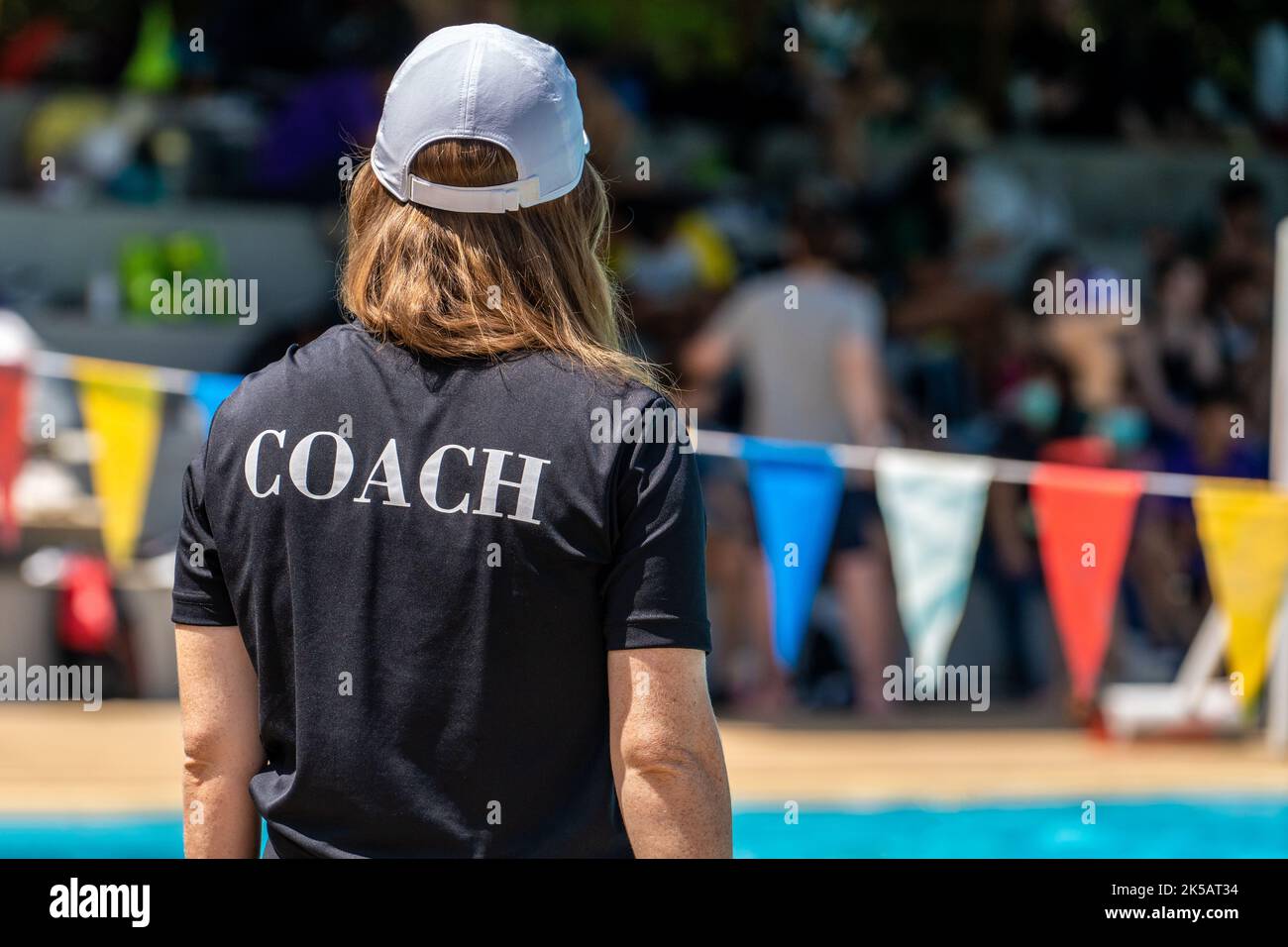Back View Of Female Swimming Coaches Wearing Coach Shirt And White Cap