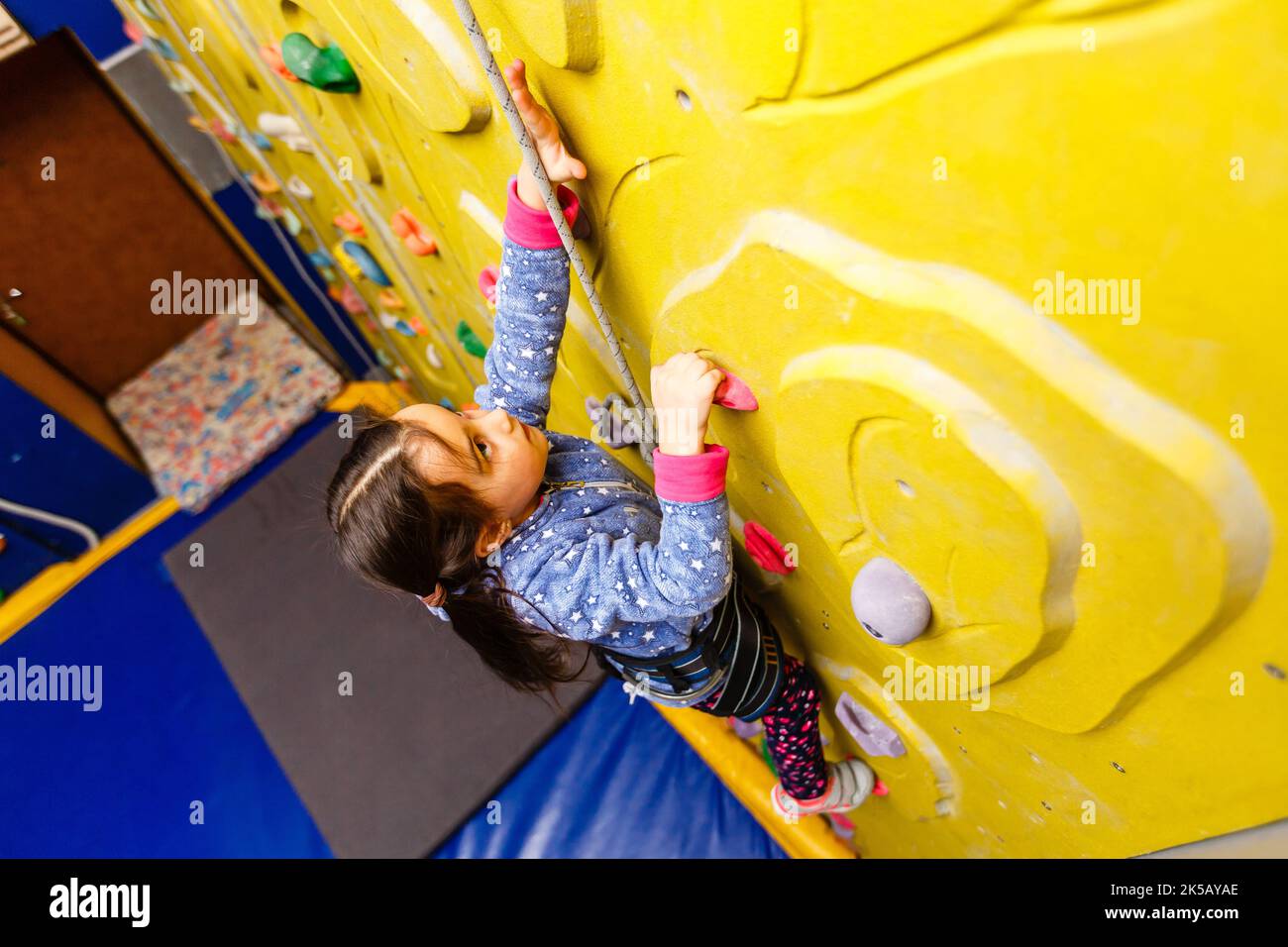 Little girl climbing a rock wall indoor Stock Photo - Alamy