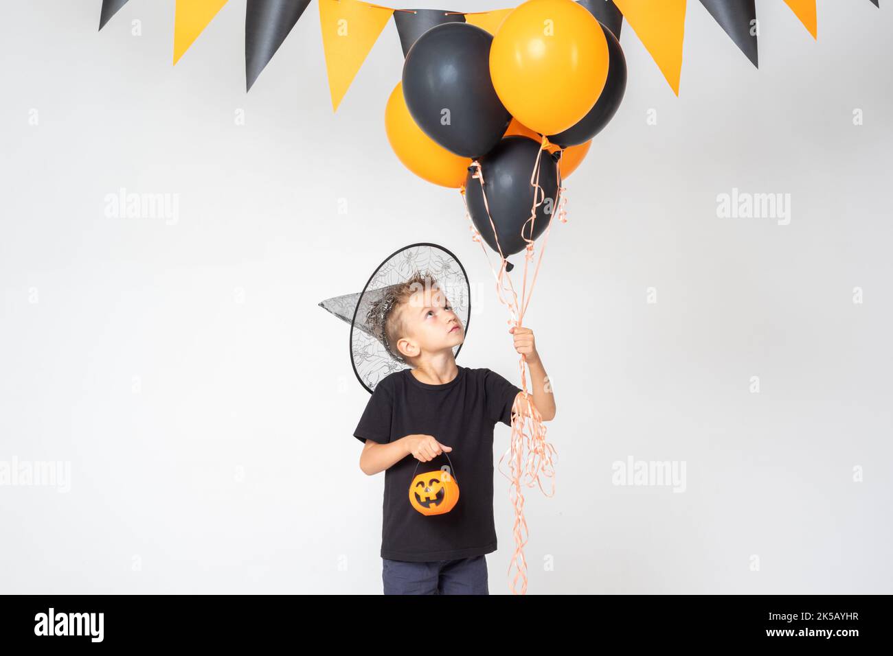 A cheerful happy Halloween boy in a wizard's hat holding a pumpkin ...