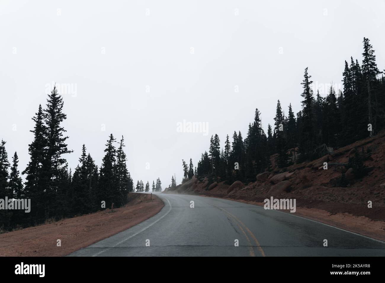 A highway asphalt road under pikes peak mountains with trees in ...