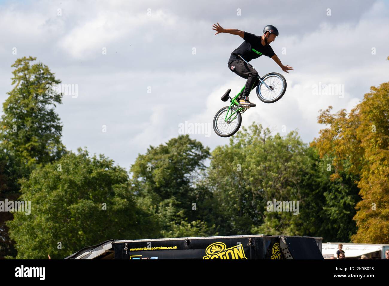 A skilled cyclist performing BMX stunts in the air in a sunny park with ...