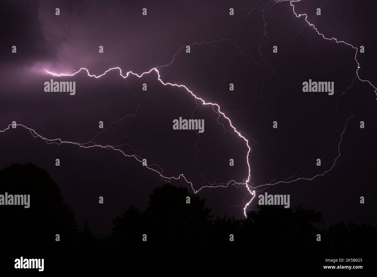 A group of lightning strikes caught on top of a forest during nighttime ...