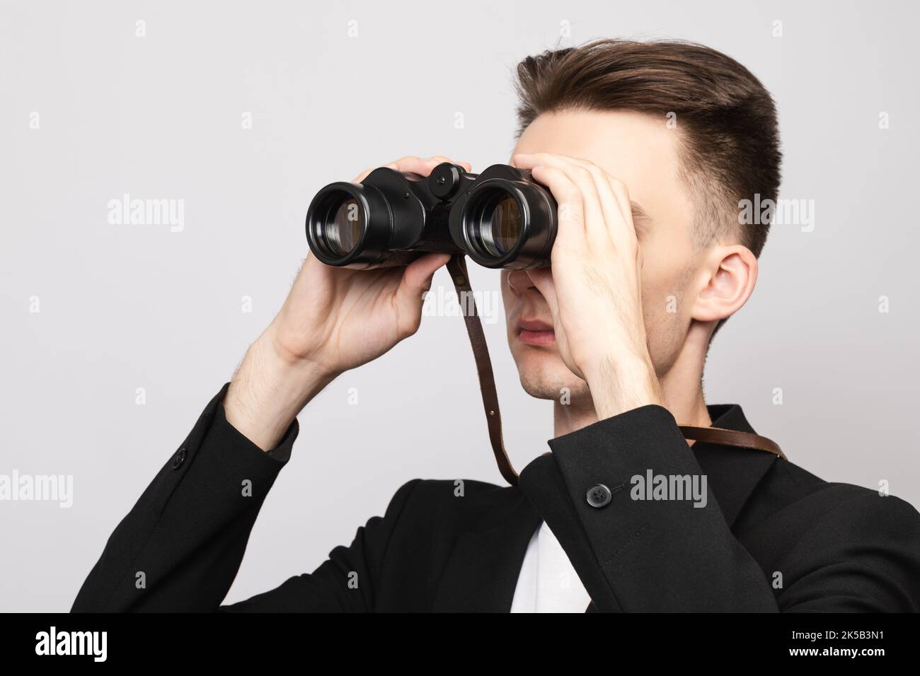 Portrait of elegant young man wearing black suit looking through ...