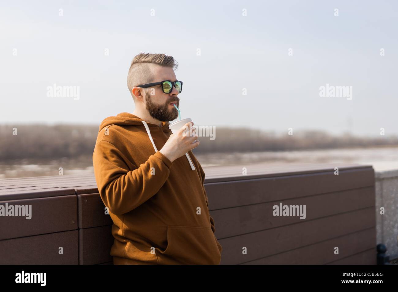 Bearded man drinking a shake in spring promenade. Drinks take away and ...