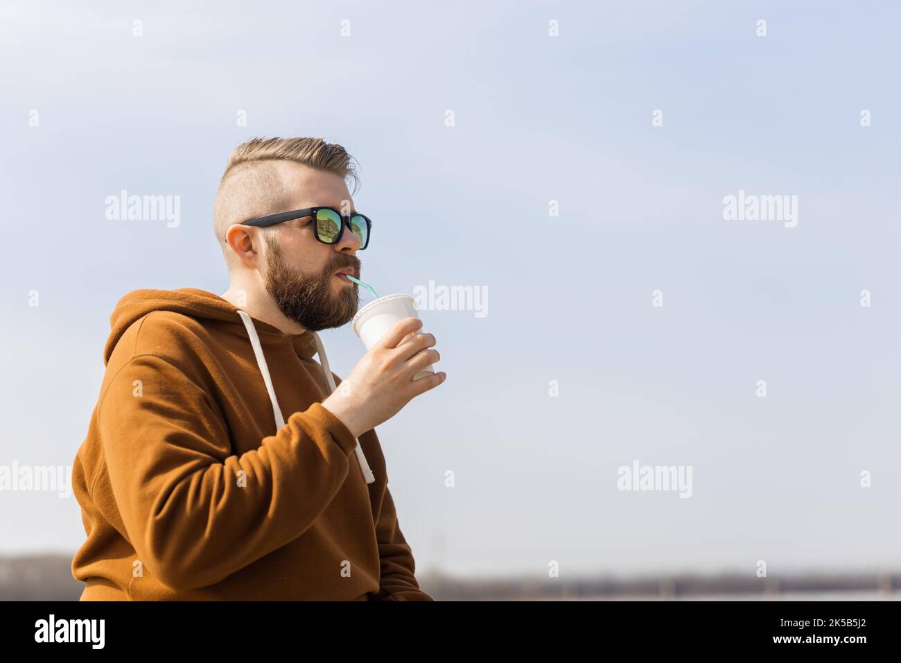 Bearded man drinking a shake sky background. Drinks take away and gen z ...