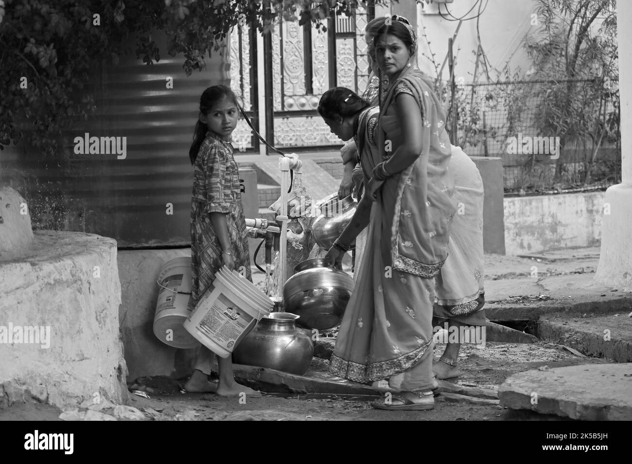 A grayscale of Indian women in traditional costumes filling buckets ...