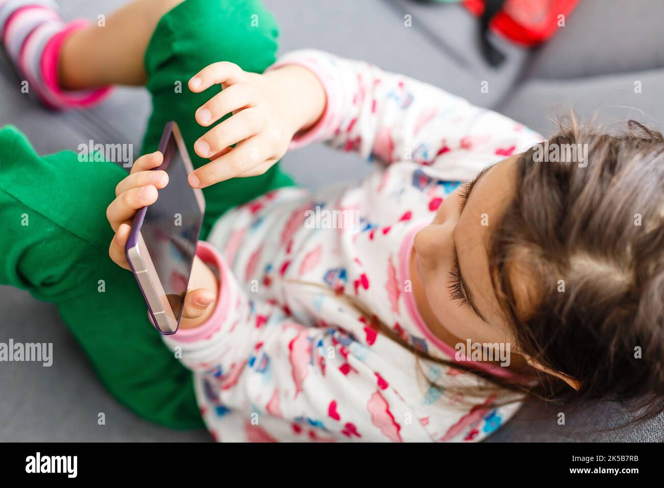 ropped shot of little girl sitting in modern home interior and using ...