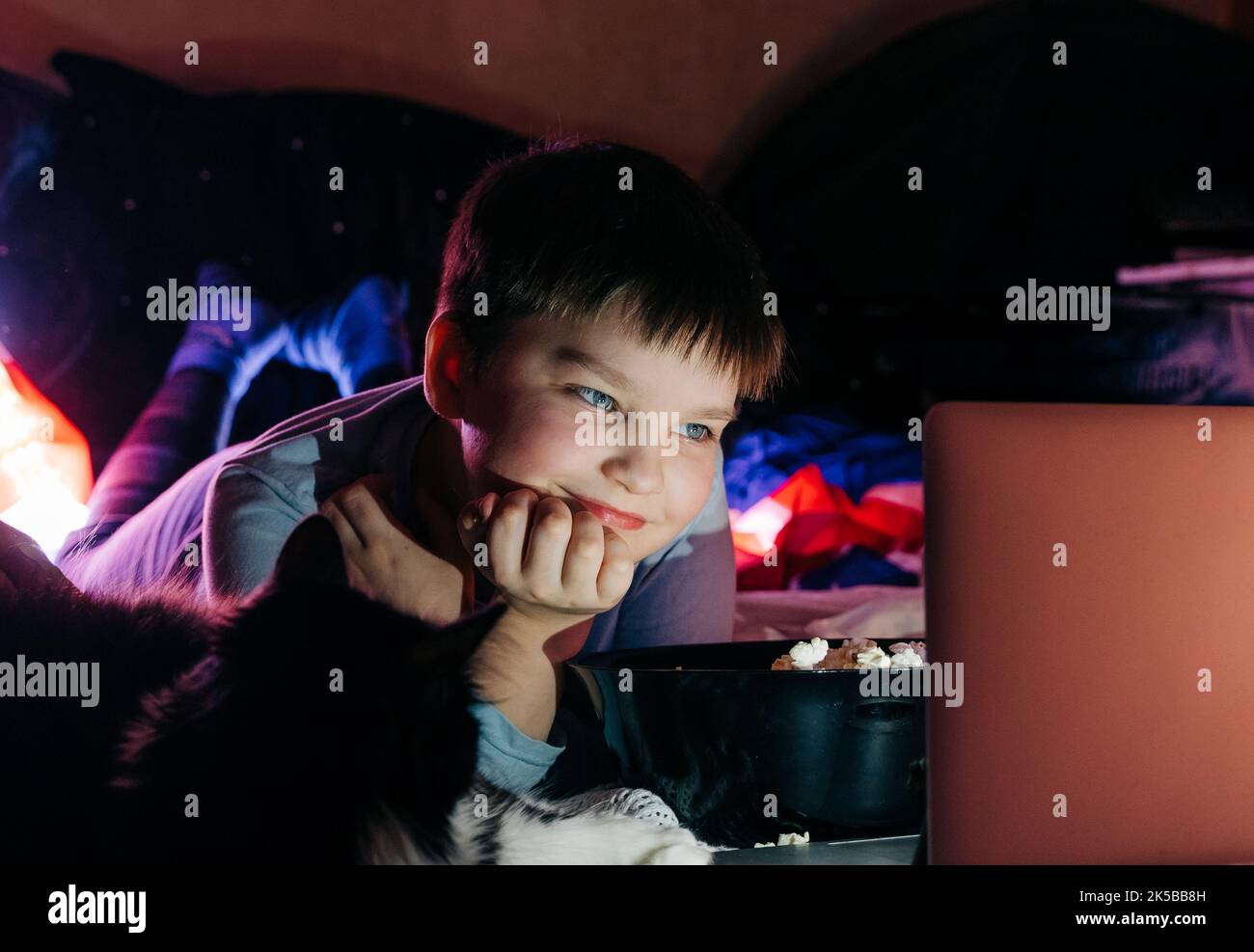 Cheerful teen boy using laptop at home watching funny movie cartoon eat ...