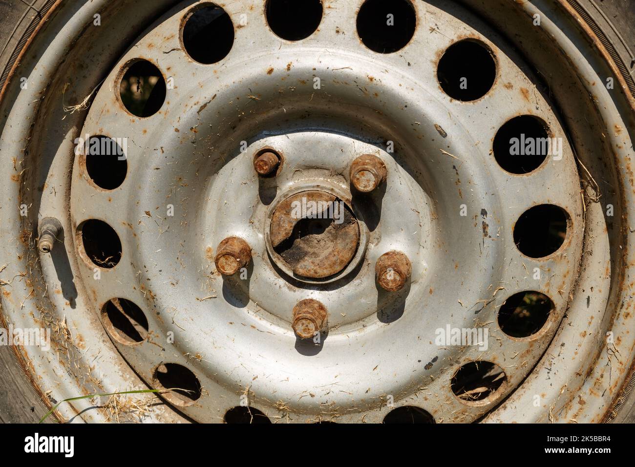 old rusty wheel in the sunlight. wheel rim, bolts and capped schrader ...