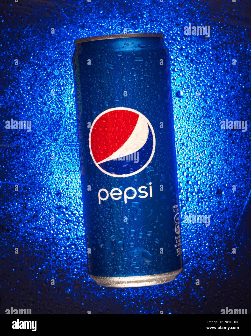 A vertical closeup of a Pepsi can on a blue background with water drops ...