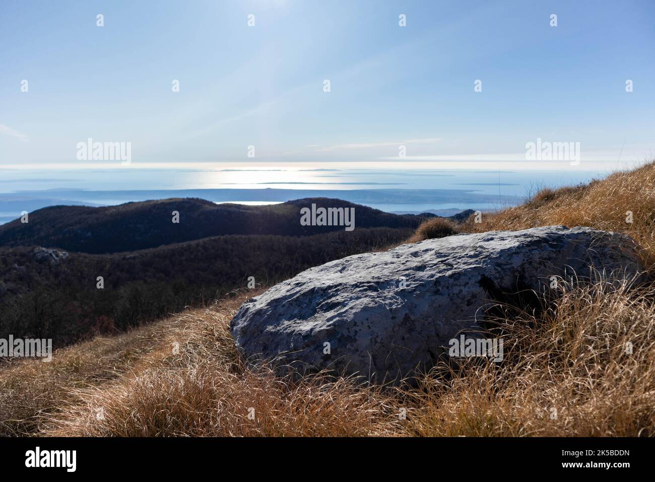 A closeup of a smooth stone on the yellow grass, mountain range and sun ...