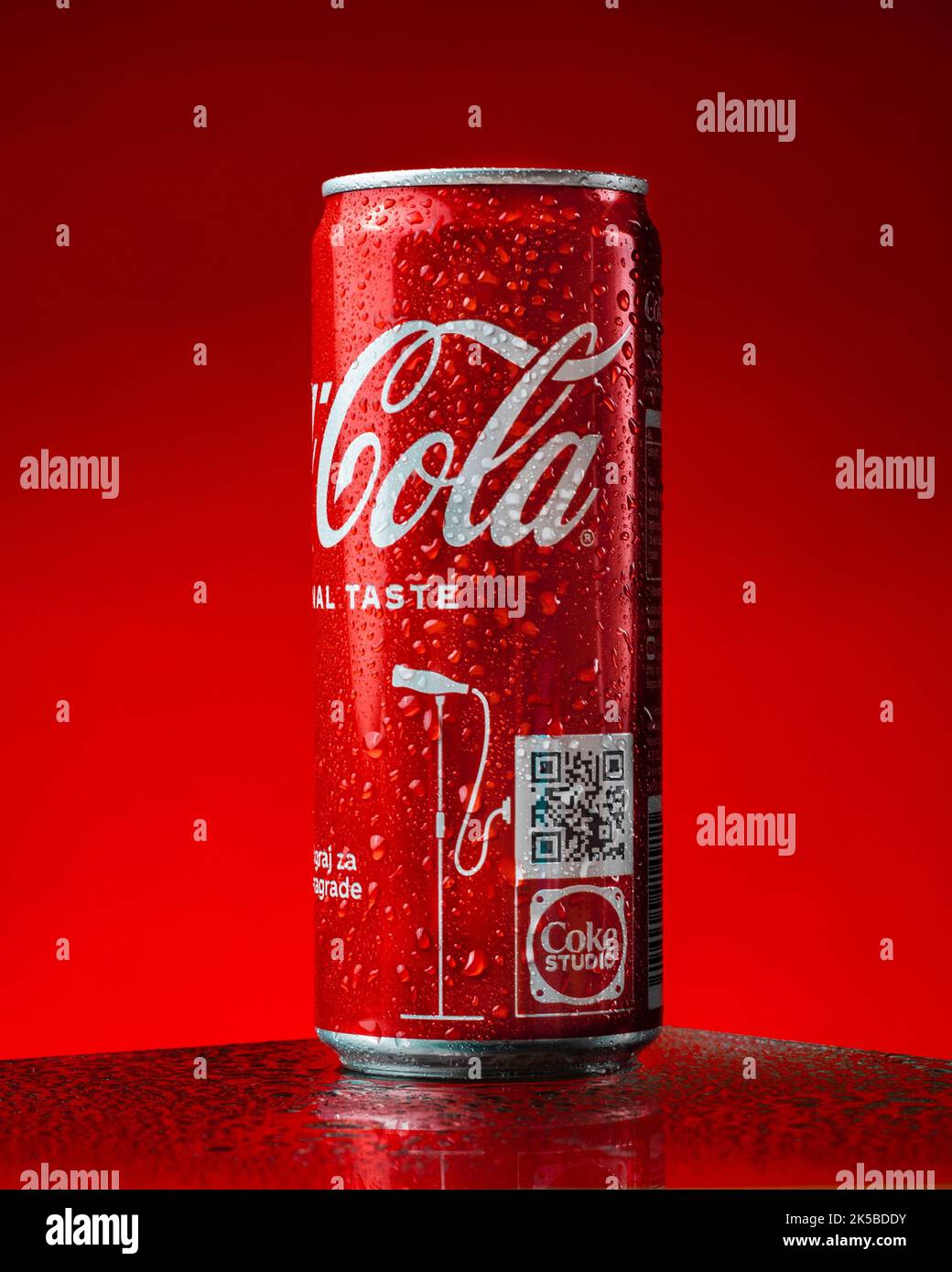 A vertical closeup of Coca Cola can on a red background with water ...
