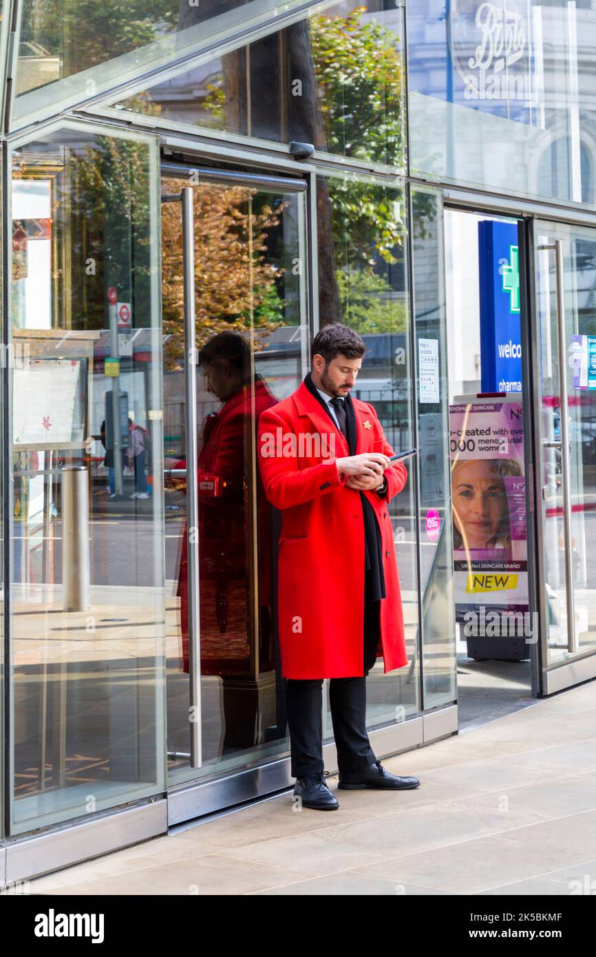 Man in red coat standing outside door entrance to Boots store in London ...