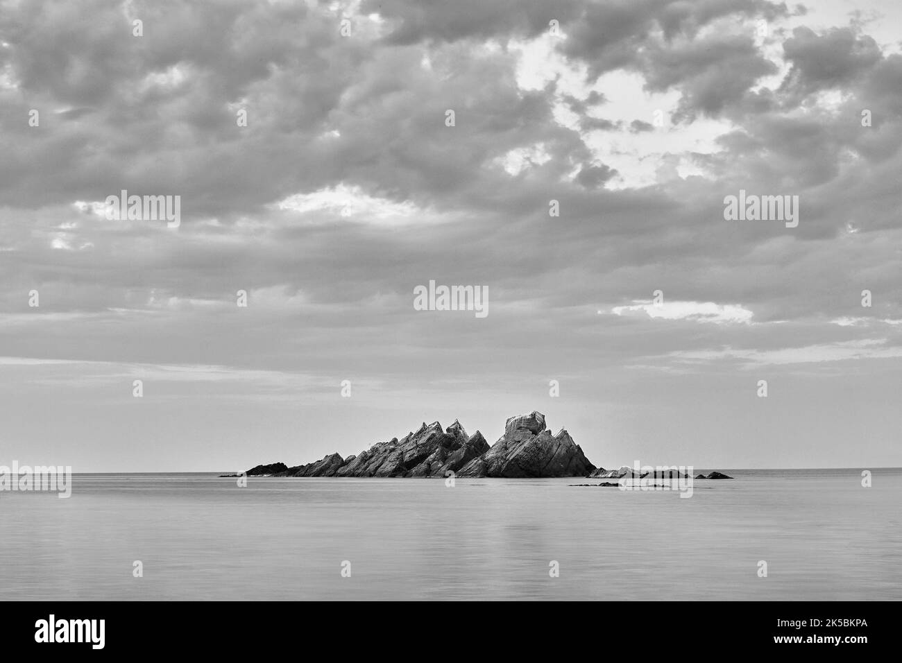 A grayscale shot of the sea with rocks against the background of the ...