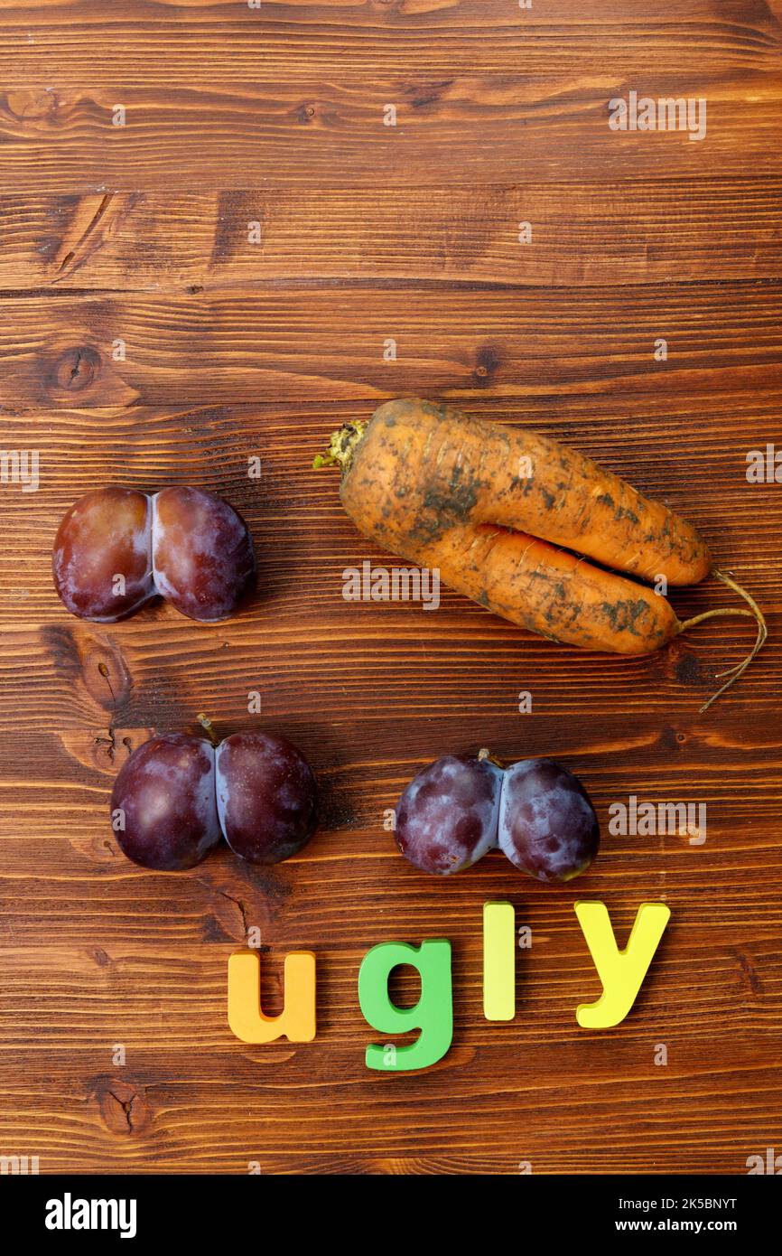Ugly organic blue plums and carrot on wooden background. The ugly ...