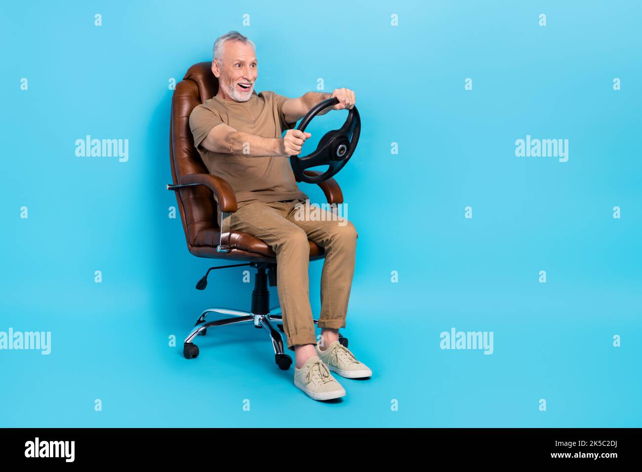 Full length photo of funky overjoyed man sit chair arms hold wheel look ...