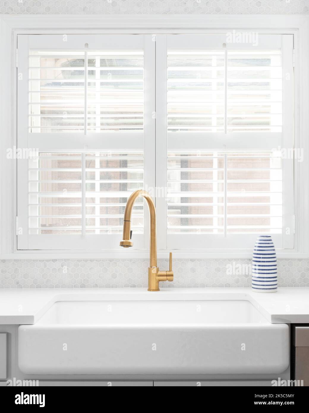 A kitchen sink detail shot with a farmhouse sink, gold faucet, grey ...