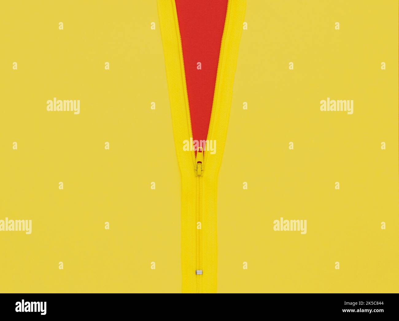A yellow zipper unzipped half way showing red color under a yellow ...